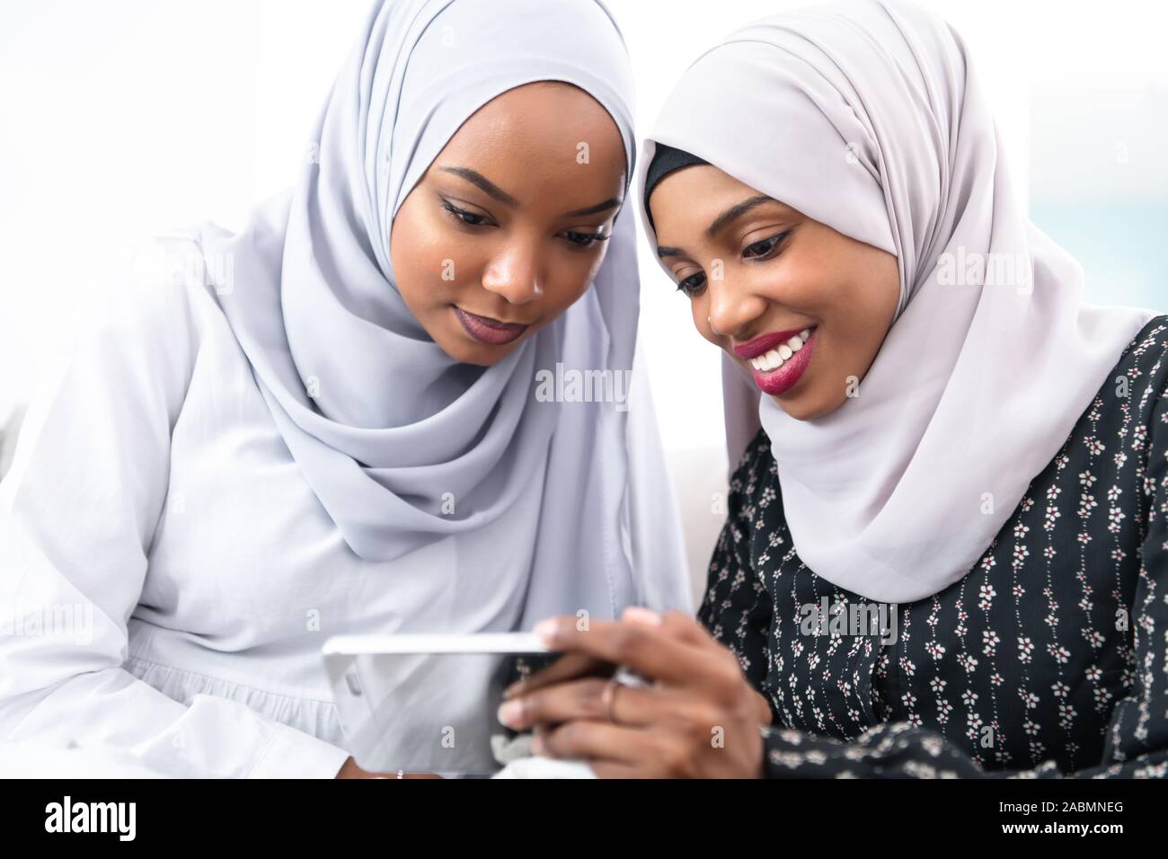 two african modern muslim women using smartphone while sitting on sofa ...