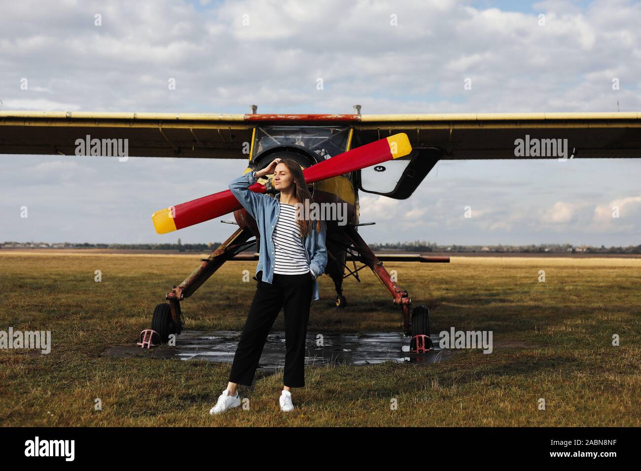 portrait of young woman near the retro plane. field with plane flying ...