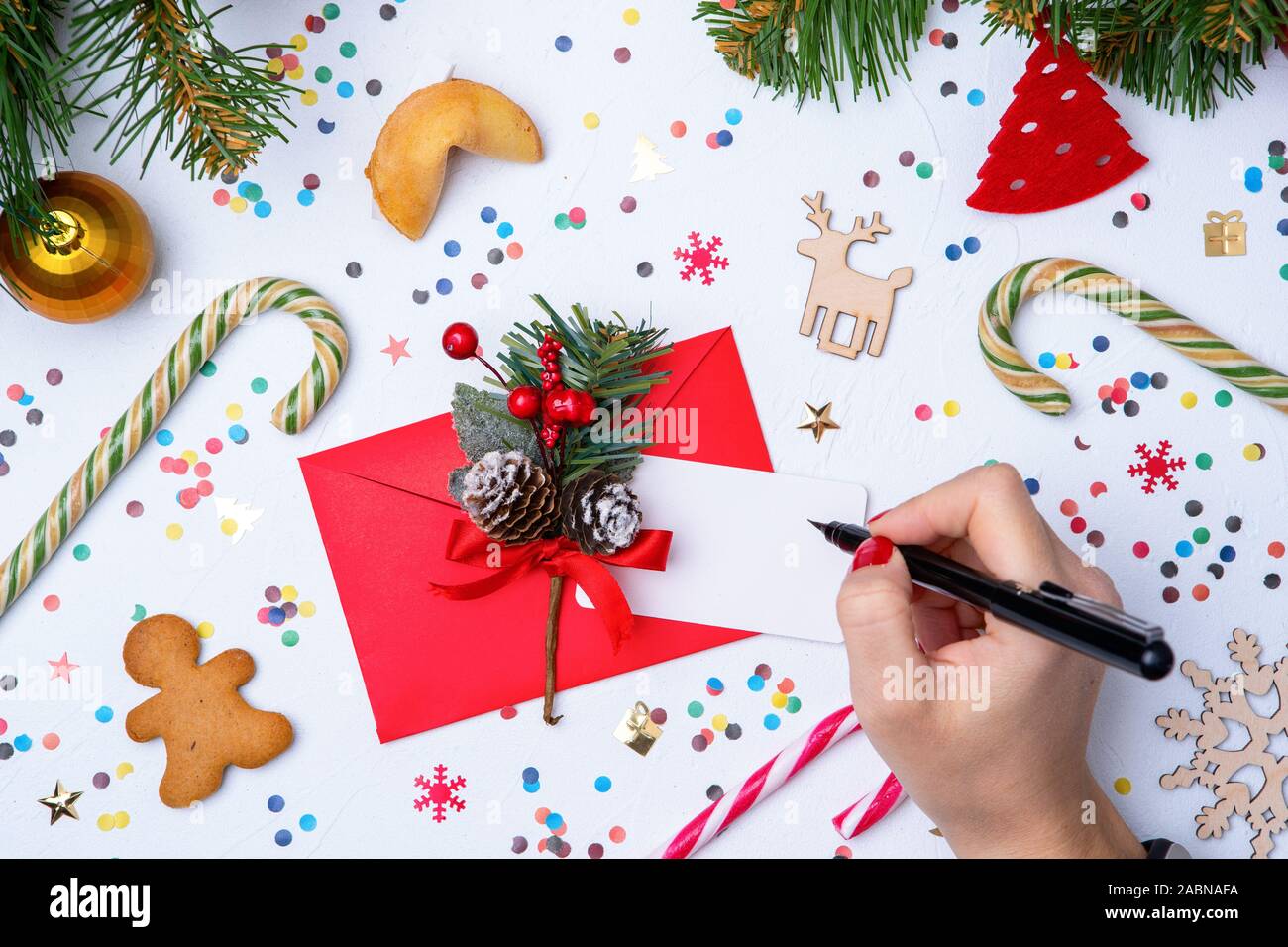Photo of red Christmas envelope, cookies, hands with pen, branches of ...