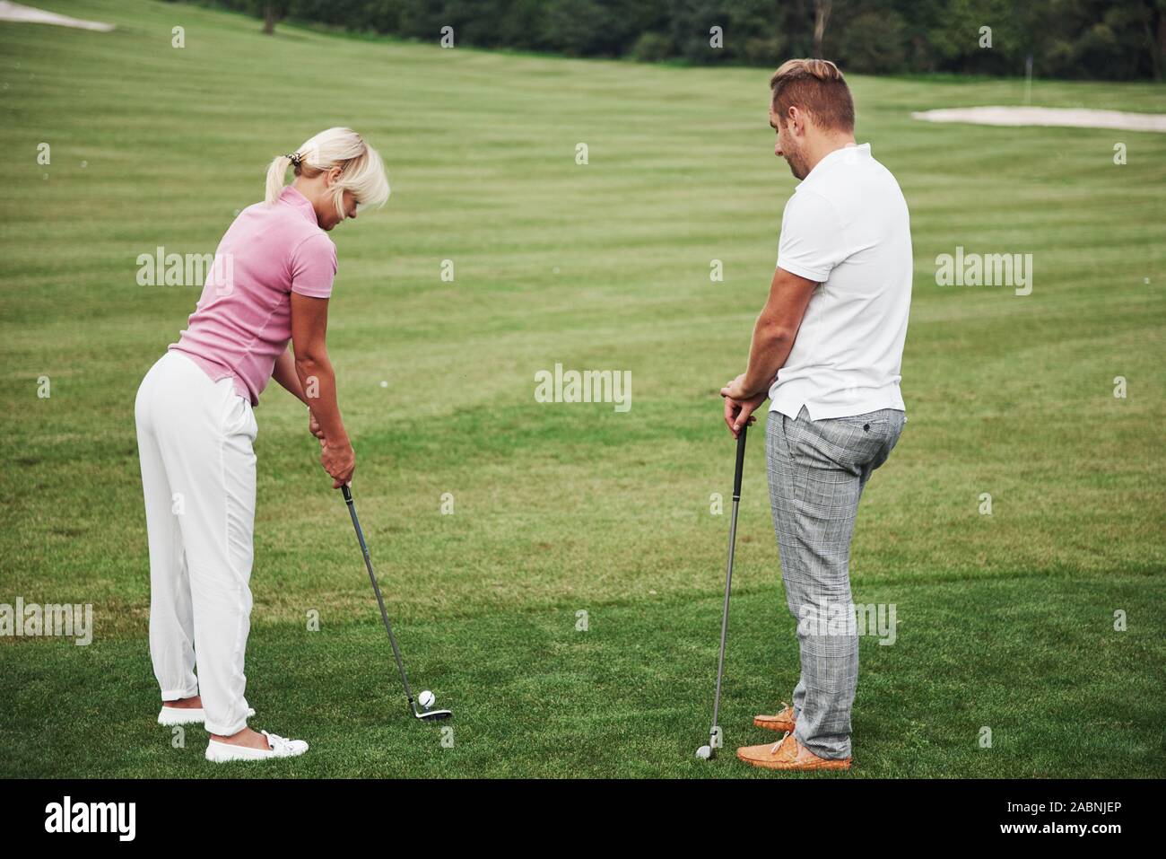 Girl playing golf and hitting by putter on green. Her teacher helps to ...