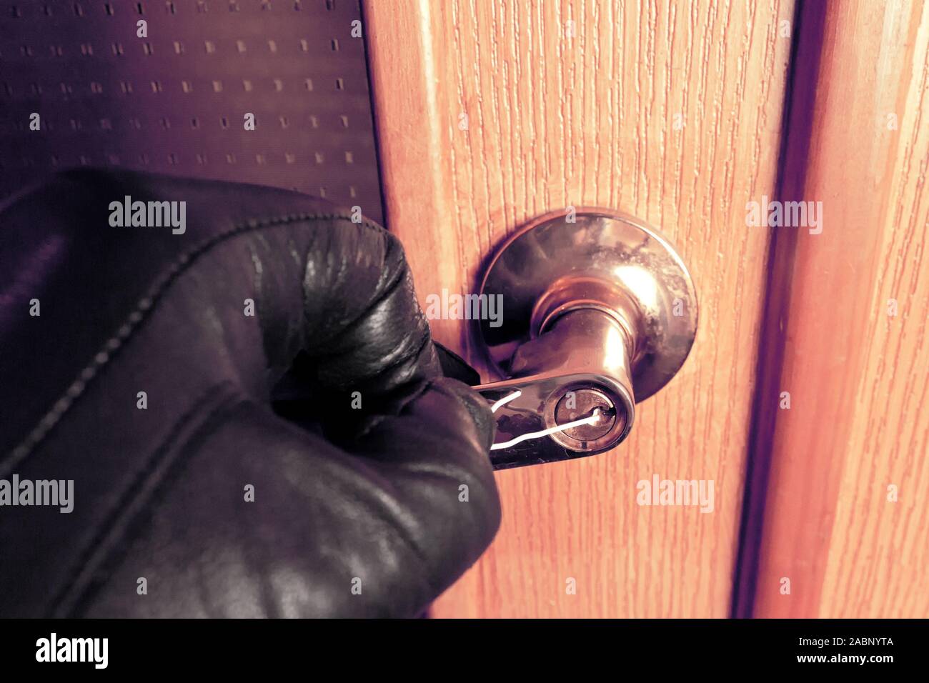 Concept home protection. Thief in black gloves opens a wooden door with ...