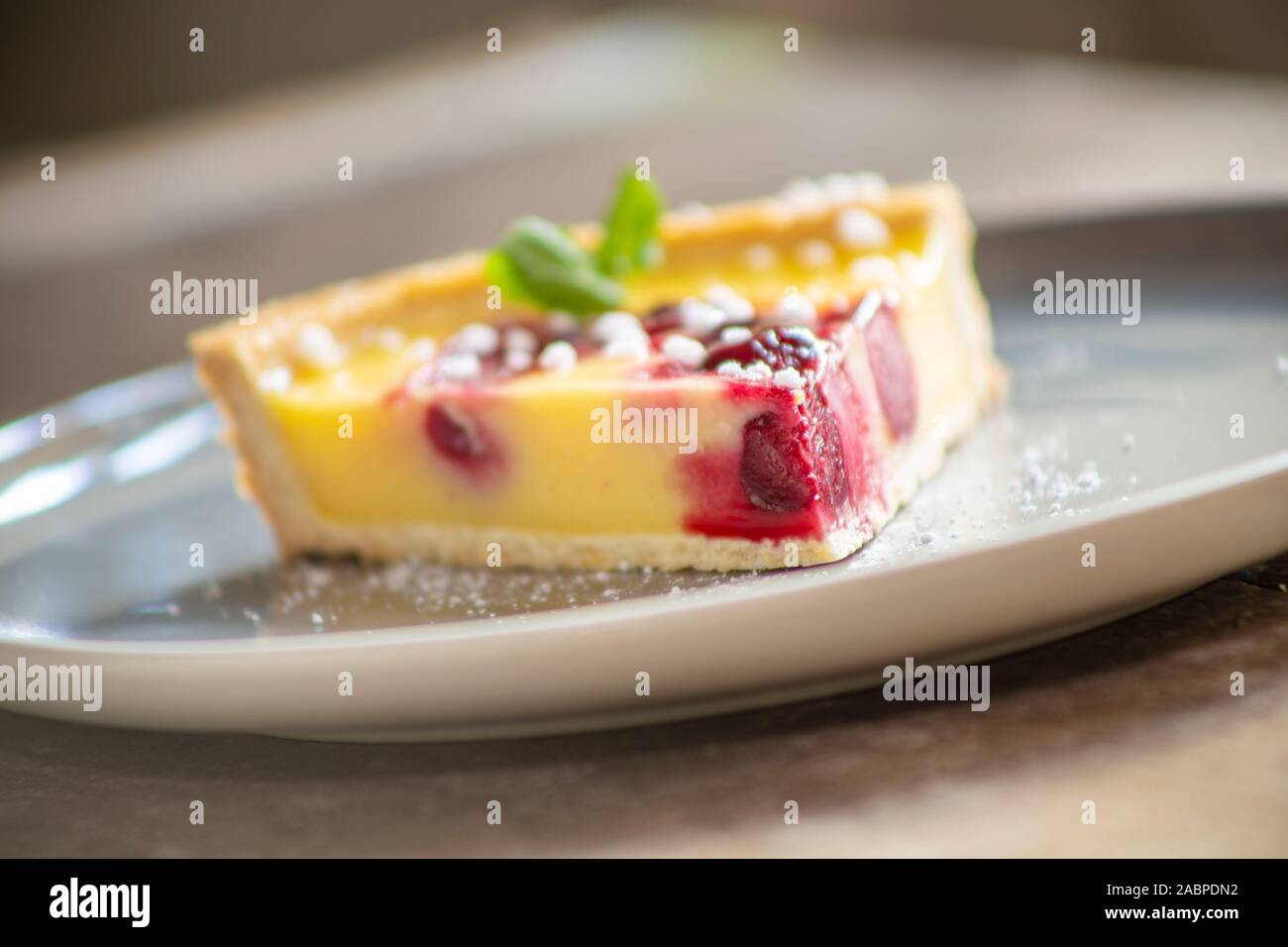 A raspberry and custard tart slice on a plate against a neutral ...
