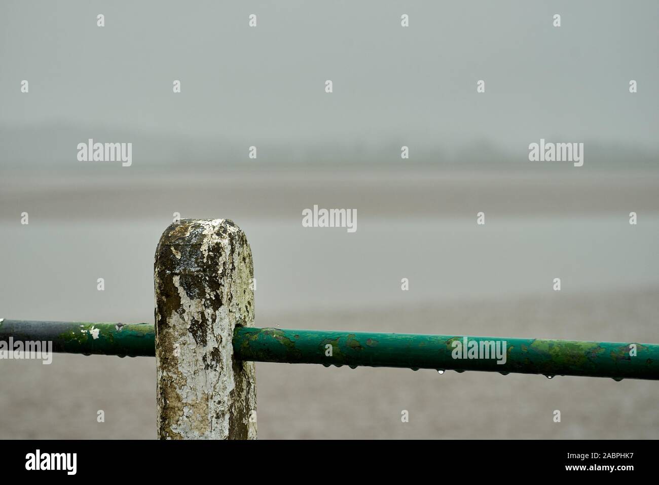 Steel railing and concrete post dripping with water with wet and murky ...