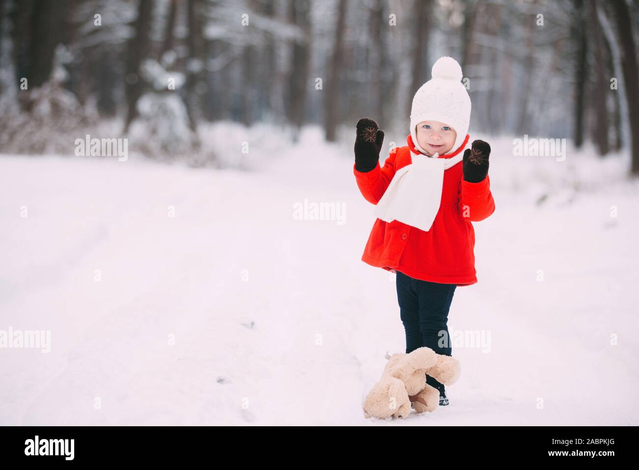 Little girl in red coat with a teddy bear having fun on winter day ...