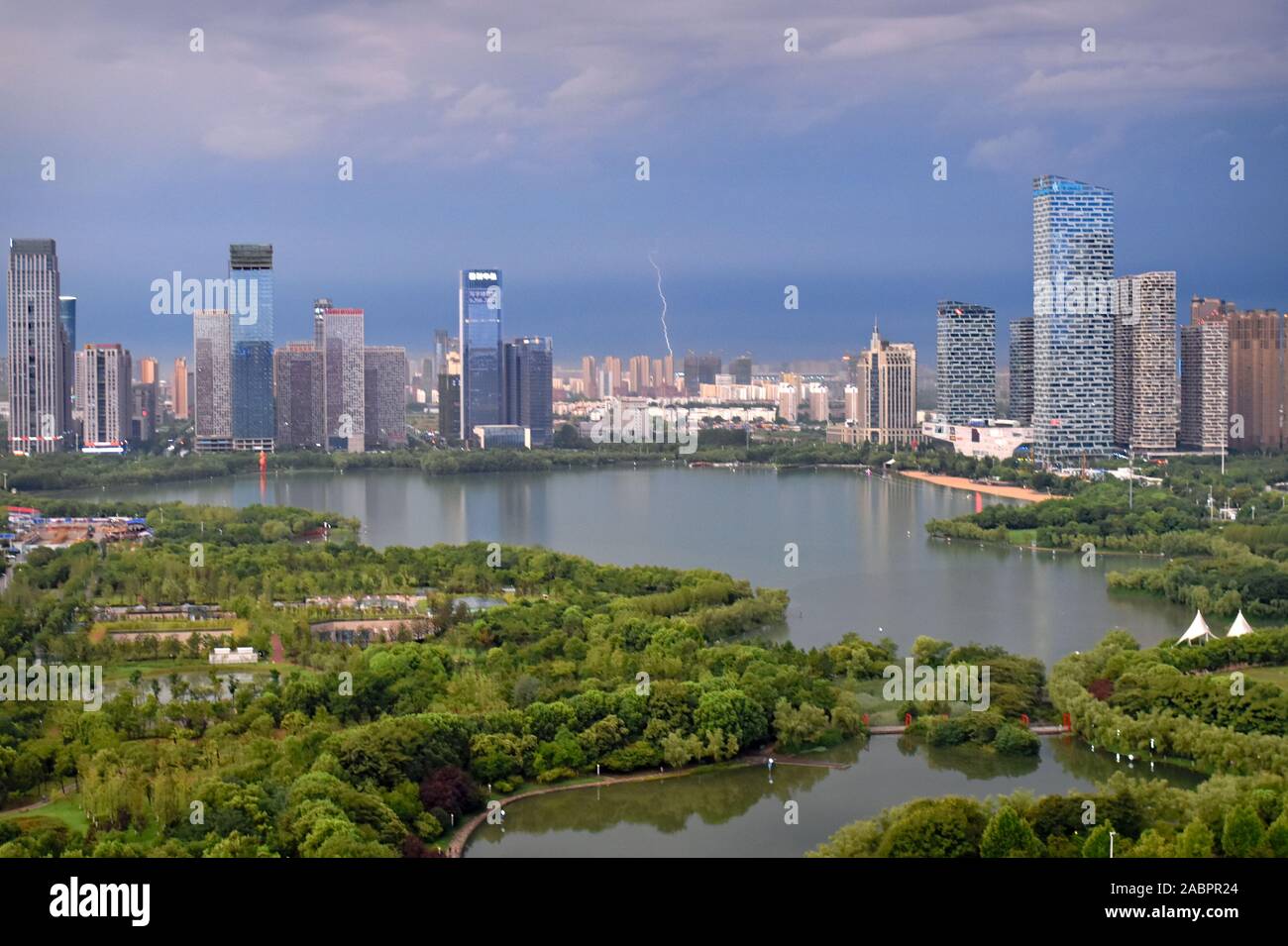 Modern Chinese city skyline by Swan lake and park during lightning ...