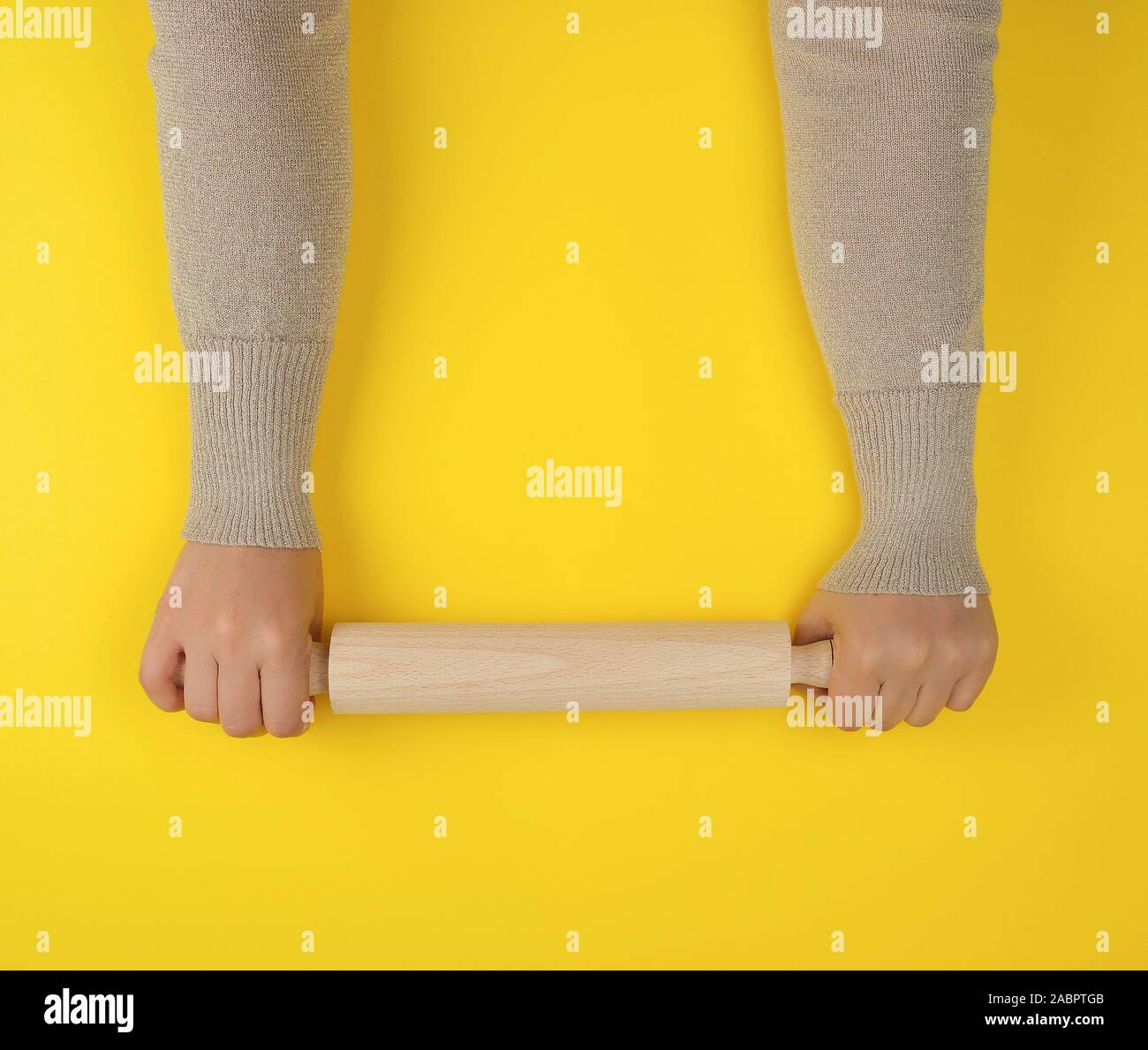 hand holding a wooden rolling pin on a yellow background, top view ...