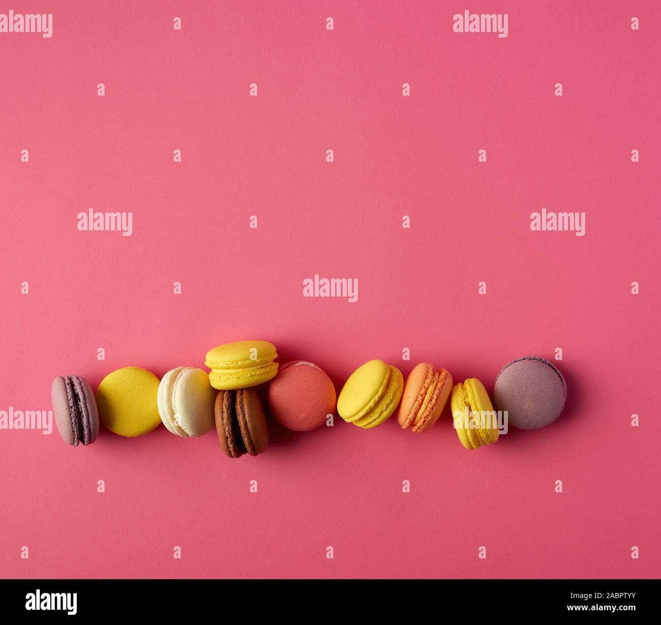 round multi-colored baked macarons with cream lie in a line on a red ...