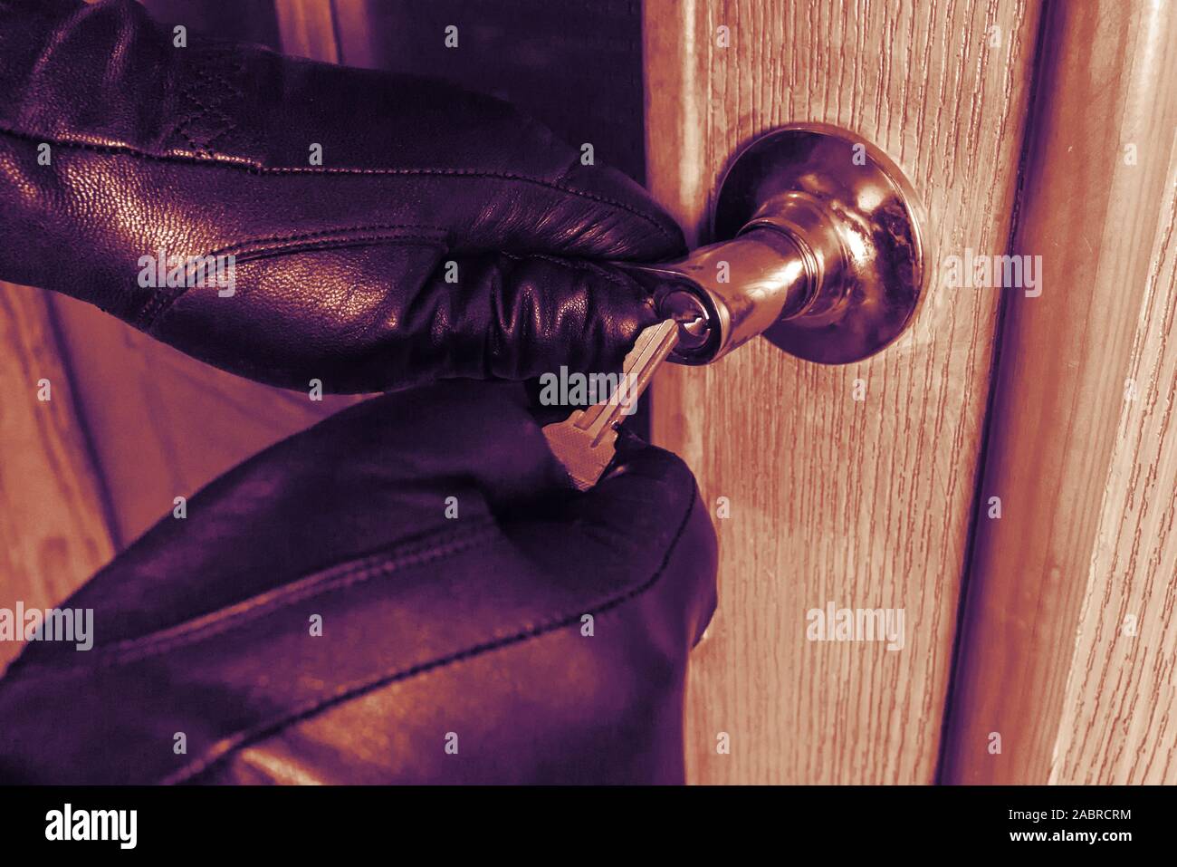 Concept home protection. Thief in black gloves opens a wooden door with ...
