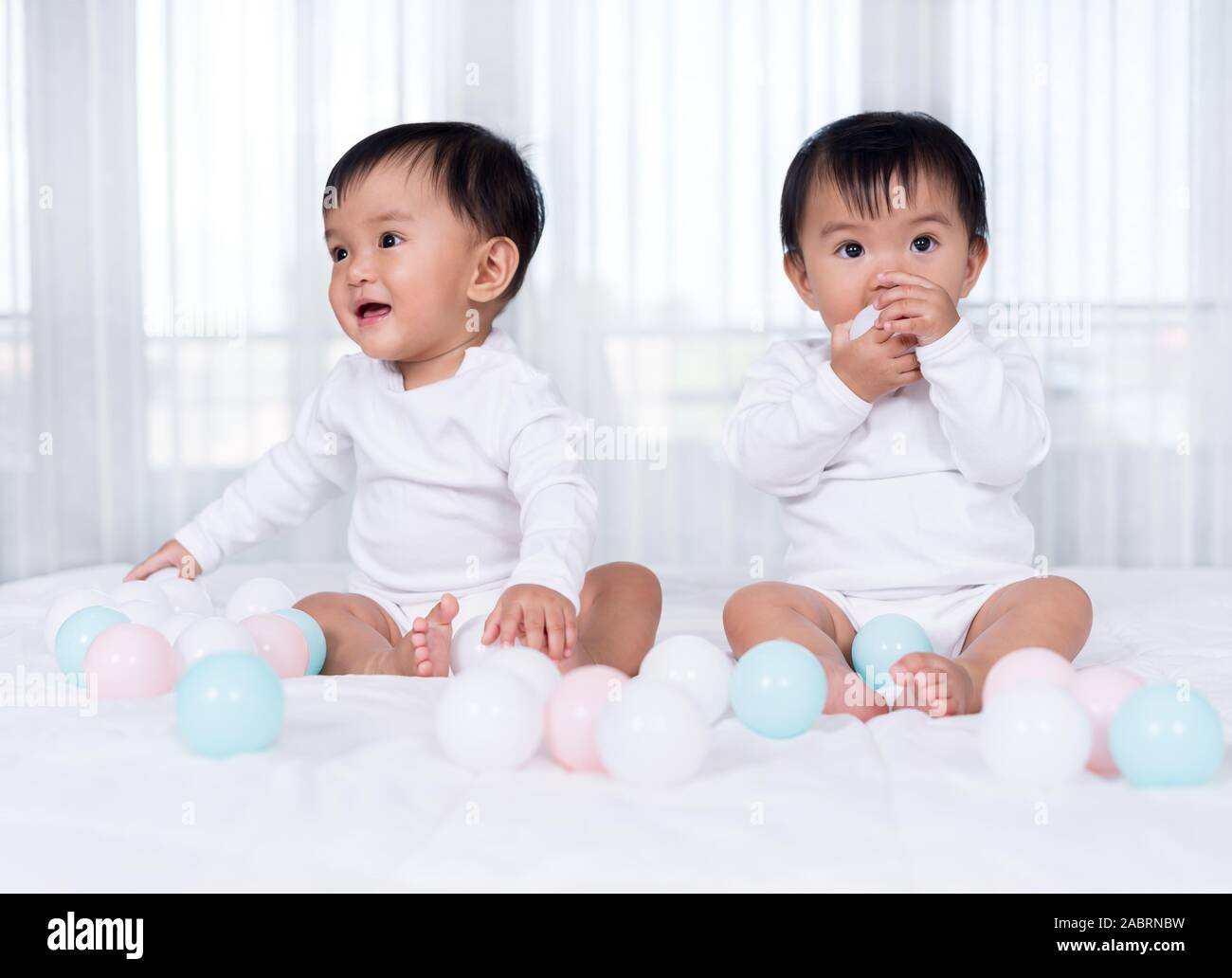 cheerful twin babies playing color ball on a bed Stock Photo - Alamy