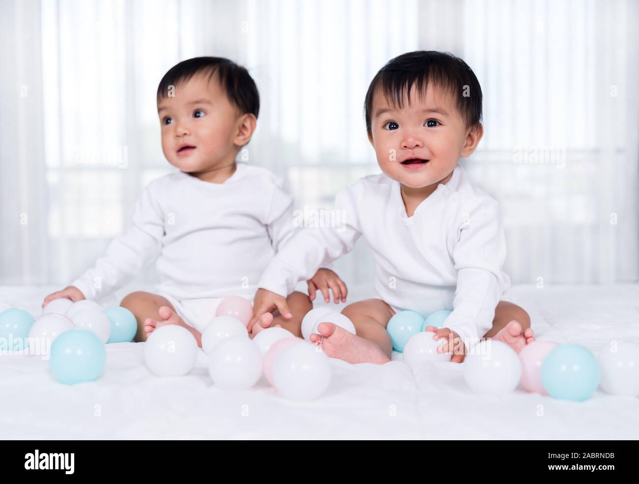 cheerful twin babies playing color ball on a bed Stock Photo - Alamy