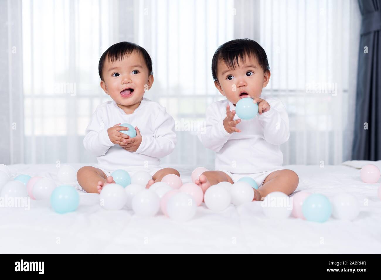 cheerful twin babies playing color ball on a bed Stock Photo - Alamy