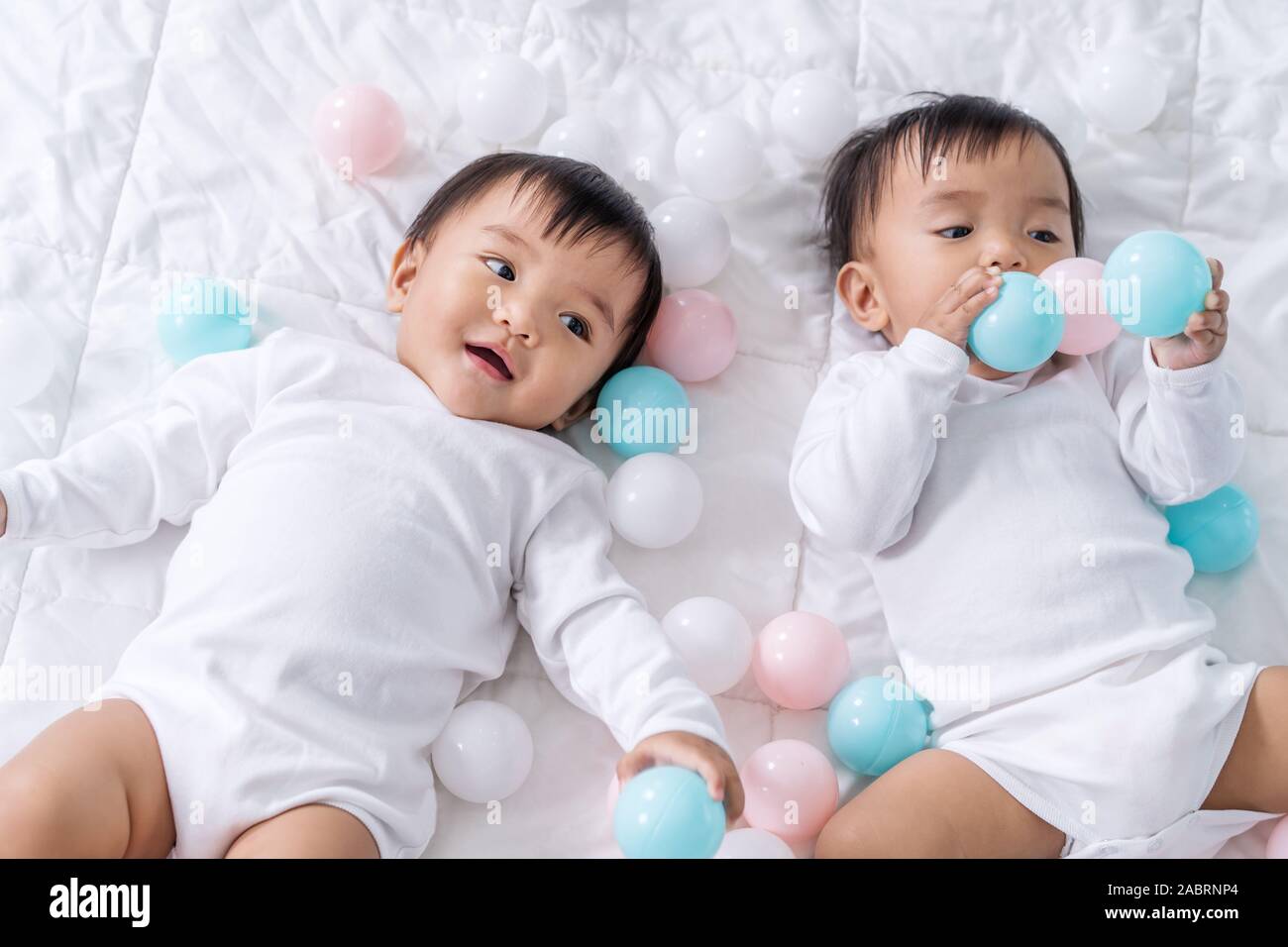 cheerful twin babies playing color ball on a bed Stock Photo - Alamy