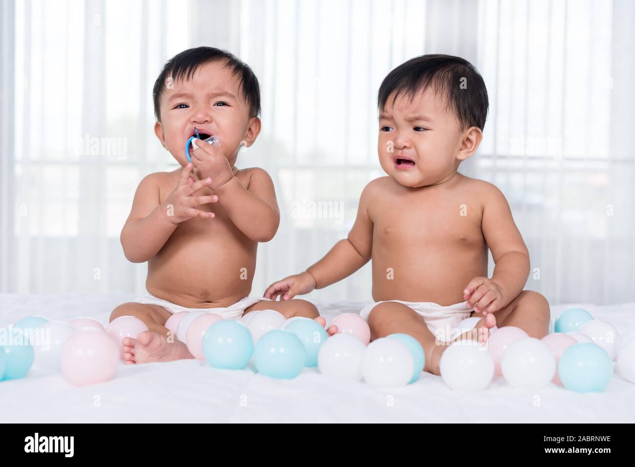 two twin babies crying on a bed Stock Photo - Alamy