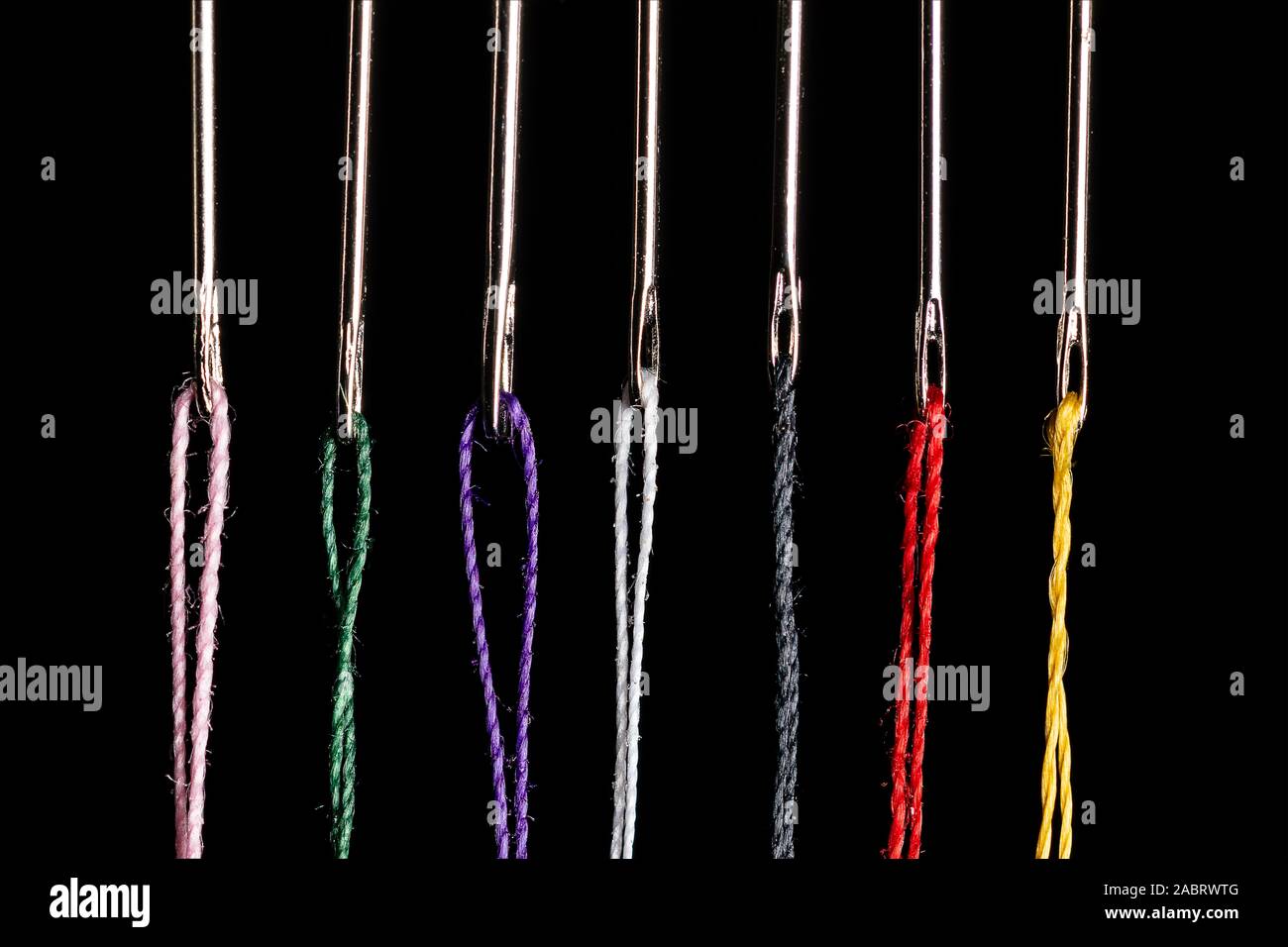 7 steel sewing needles threaded with various colored threads ready to ...