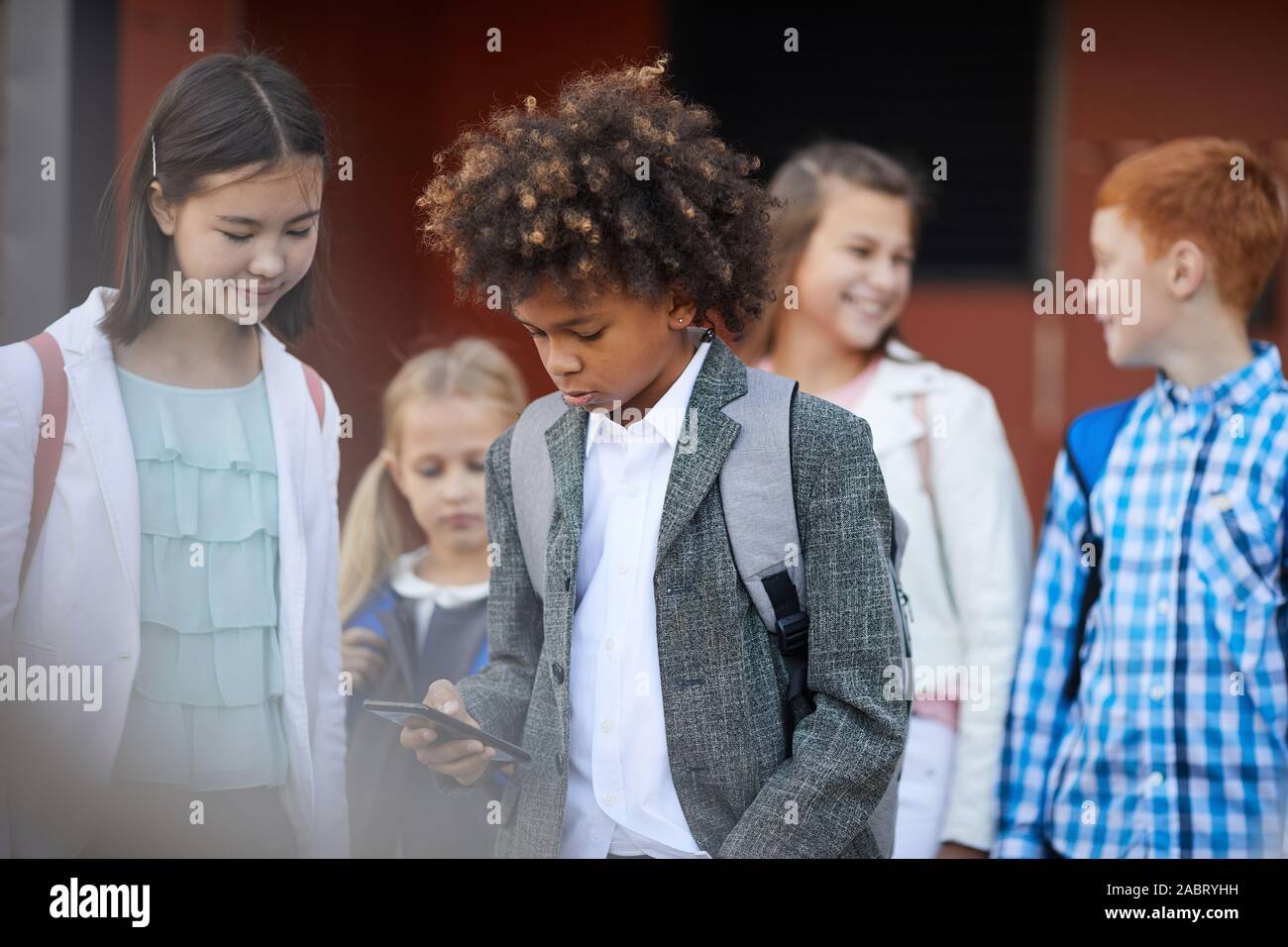 African schoolboy using mobile phone while standing with his classmates ...