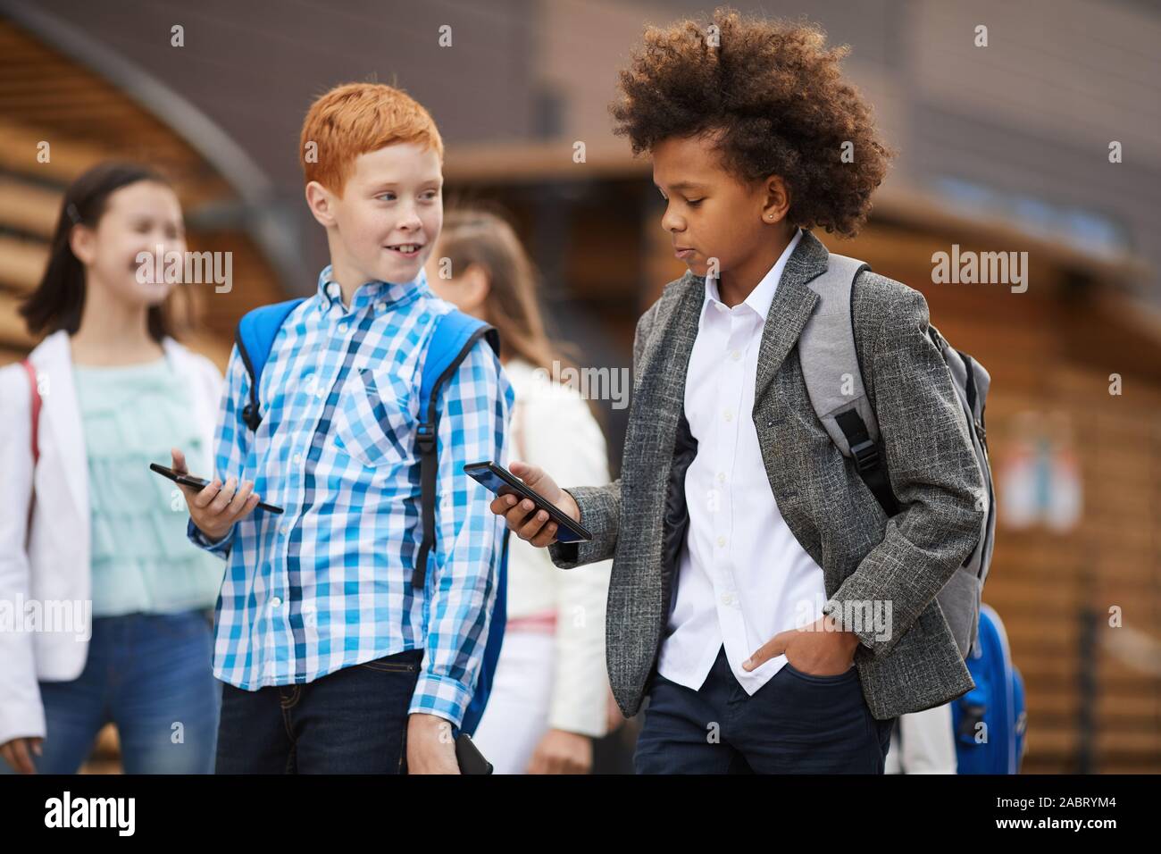 Two friends using their smart phones while walking along the street ...