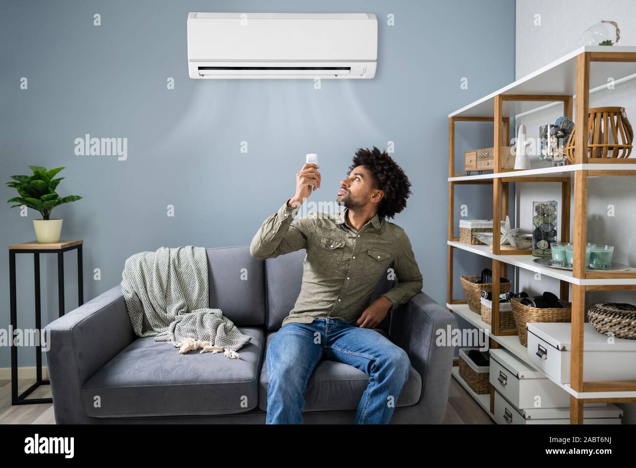 Young Happy Man Sitting On Couch Operating Air Conditioner With Remote ...