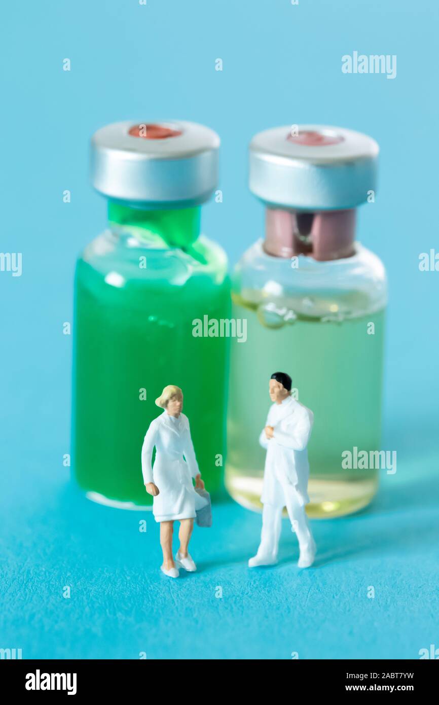 A miniature doctor standing on front of two vials with medicine in it ...