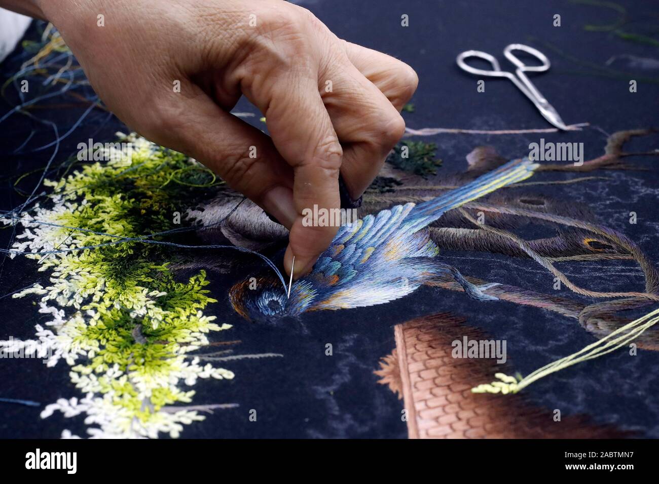 Young female workers doing embroidery. Bird. Close-up on hand. Hue ...