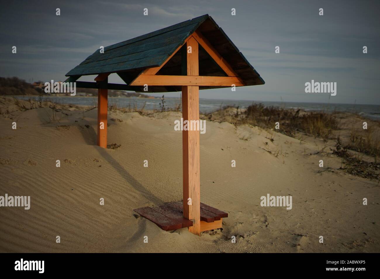 Wooden bench with a canopy covered with sand on a sea spring beach ...