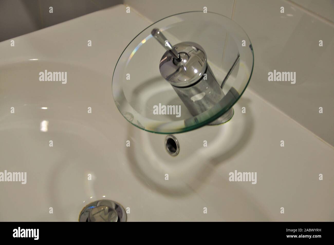 A running bathroom glass faucet with a tile and glass back splash. A ...