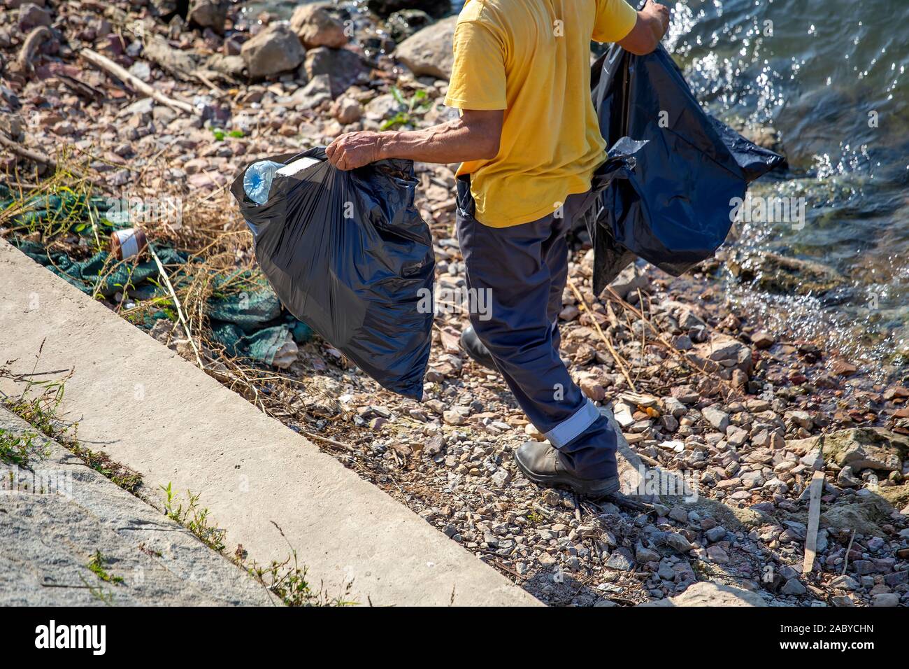 Cleaning river bank of plastic waste and other, worker picks up trash ...