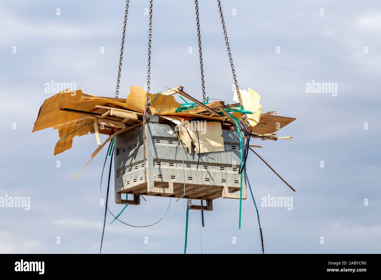 Construction crane lift basket with heap of garbage against blue sky ...
