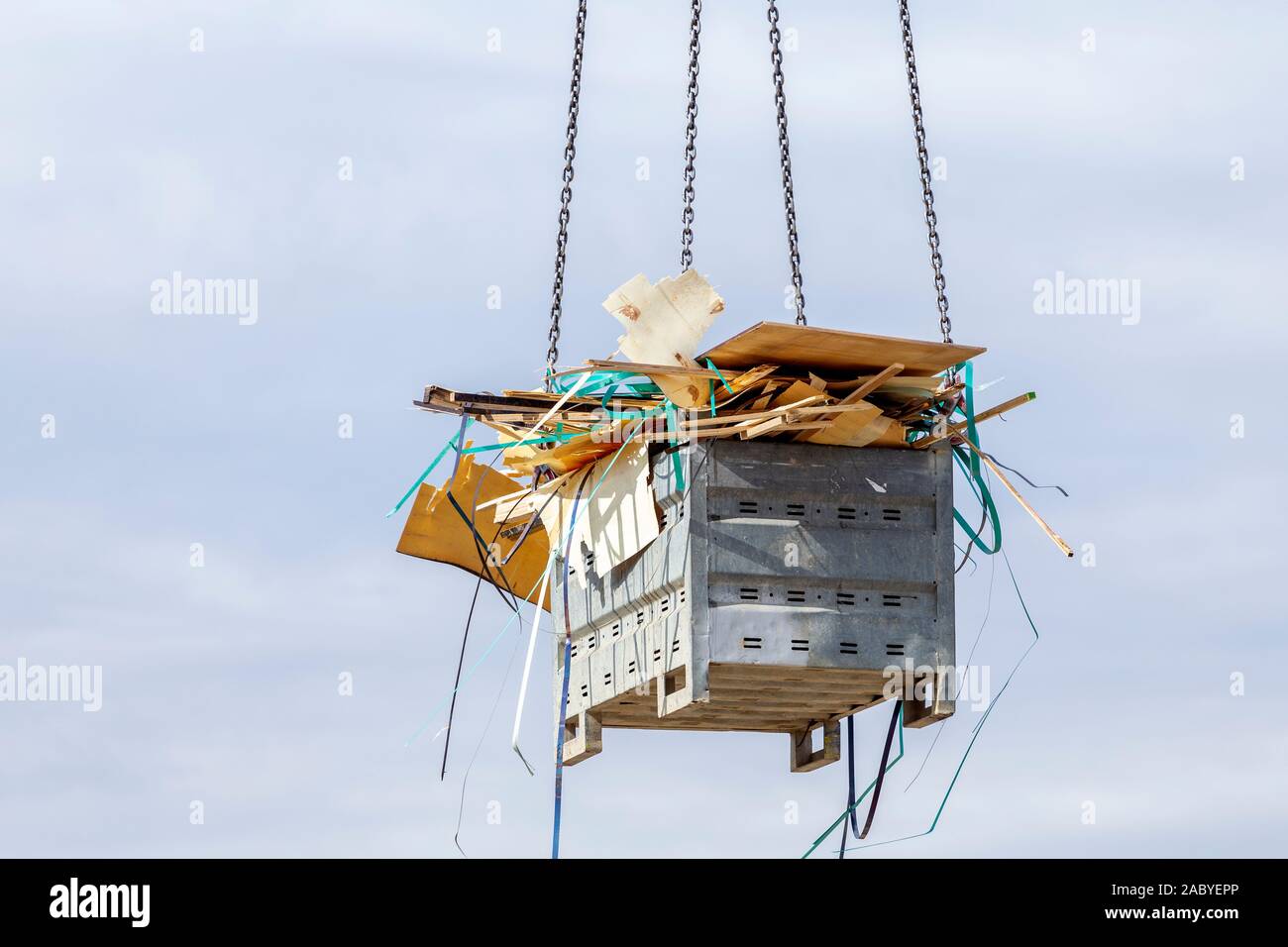 Construction crane lift basket with heap of garbage against blue sky ...