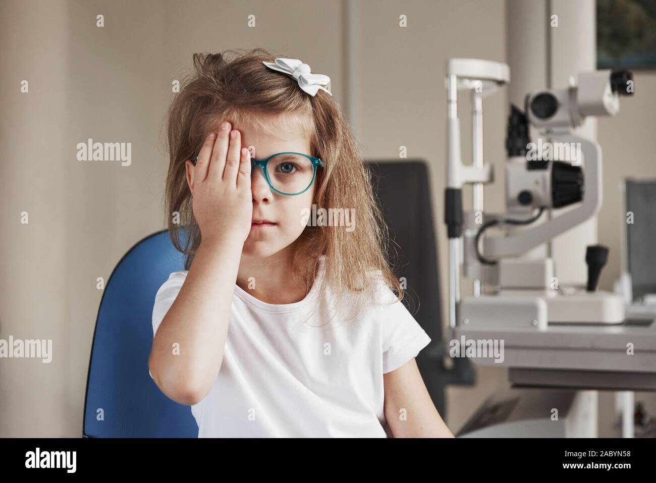 Ophthalmic equipment at background. Child closes the right eye with his ...