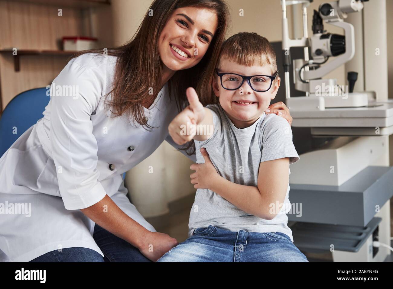 Joyful and happy. Female eye doctor sitting with the kid after doing ...