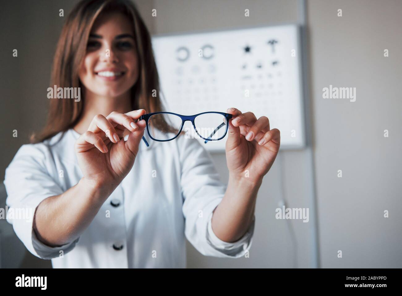 Female doctor standing in the office and holding eyeglasses with board ...