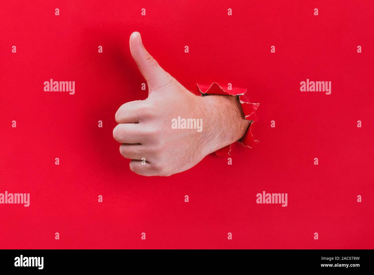 Male hand breaks through the red paper background and shows his thumb ...