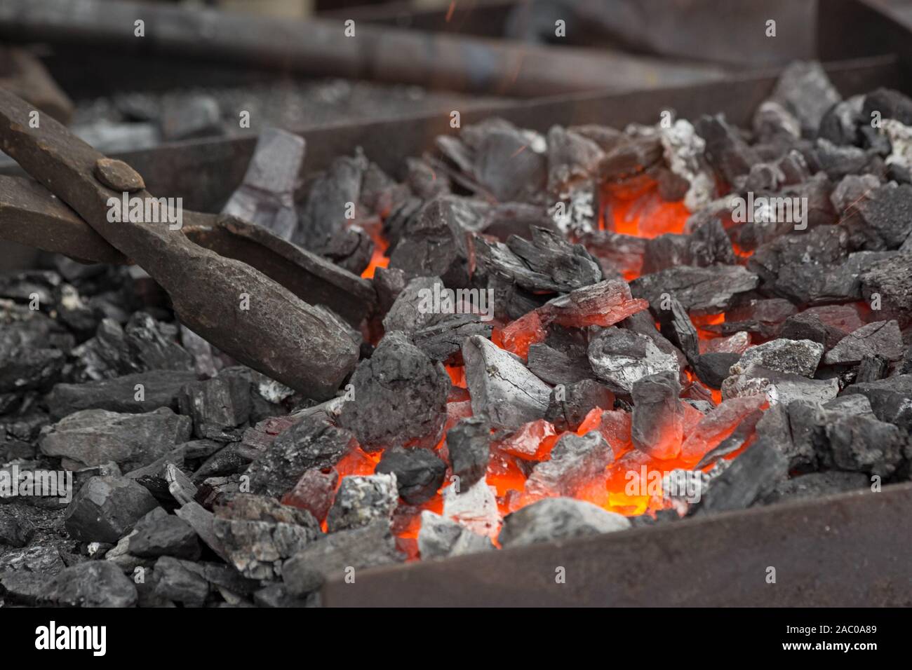 A blacksmith sets up the brazier with embers with large coal tongs ...