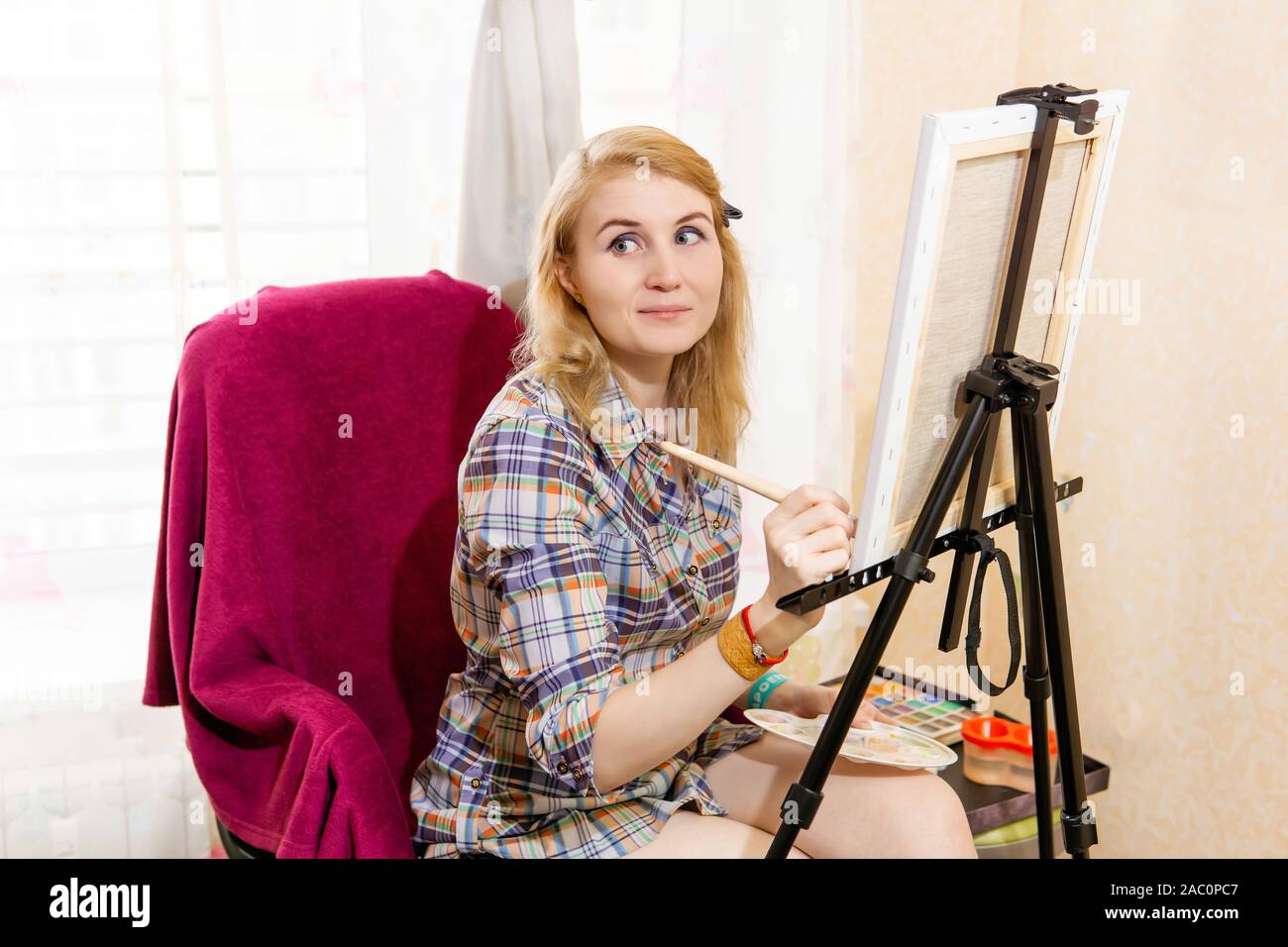 female artist paints behind an easel, looking sideways at a model ...