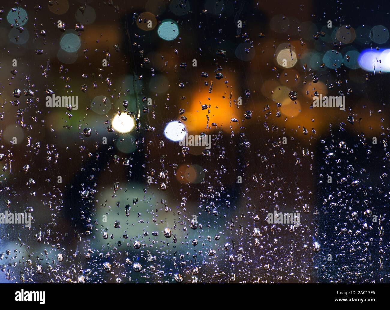 Rain outside. Drops of water on a window pane at night. Bad weather in the city. Lantern light ...