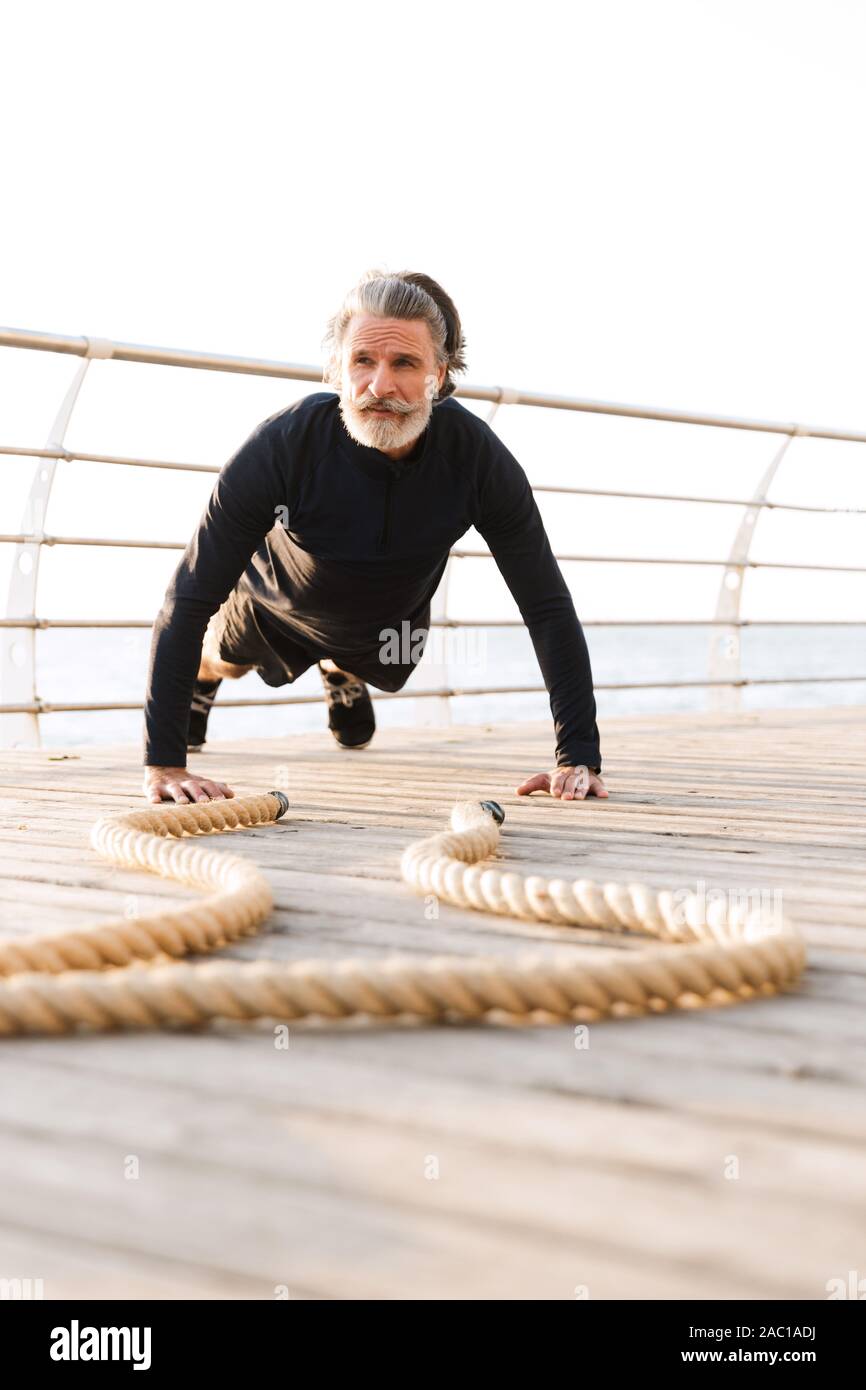 Image of caucasian old man in tracksuit doing exercise with battle ...