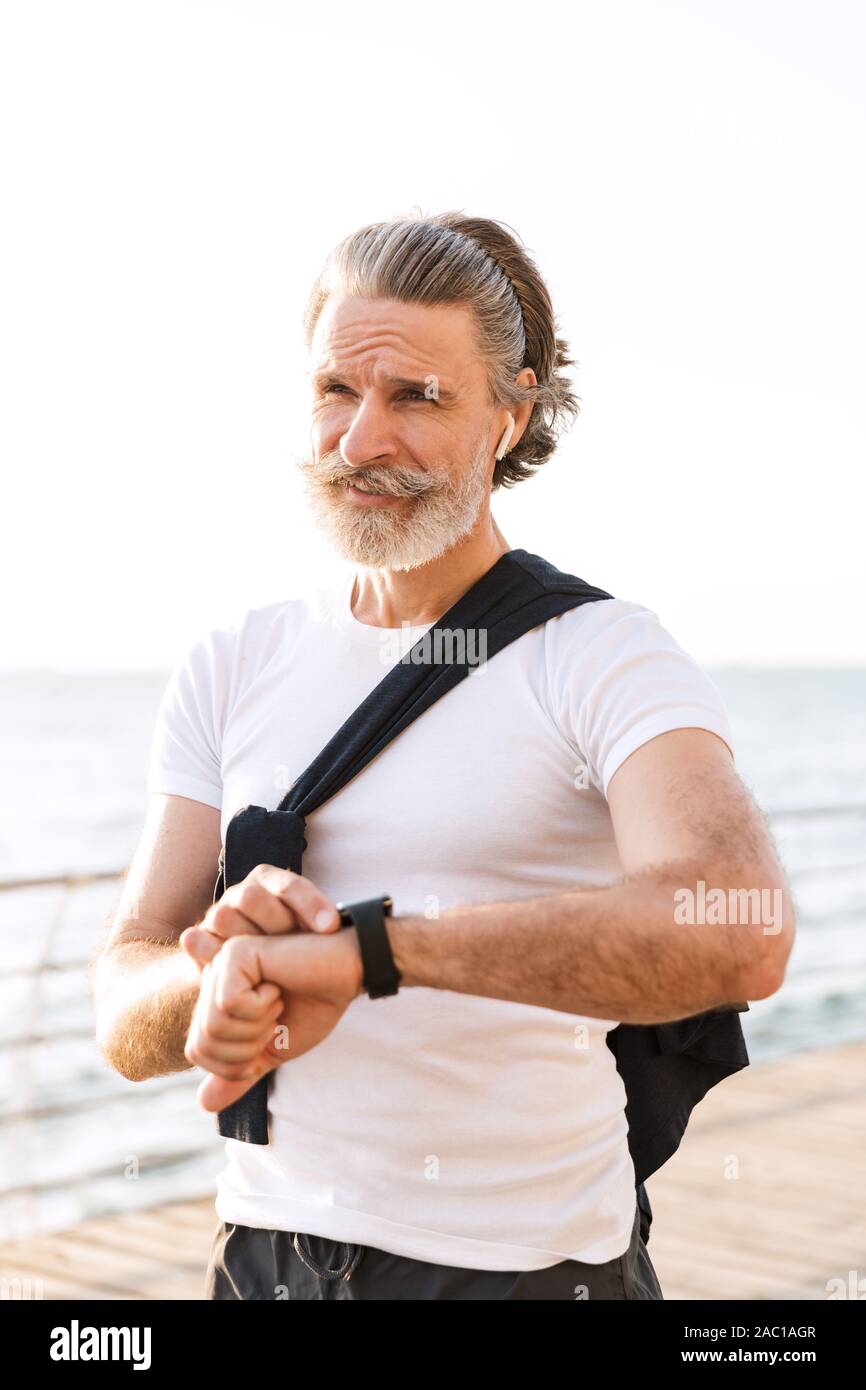 Image of joyful elderly man in sportswear using smartwatch and earpod ...