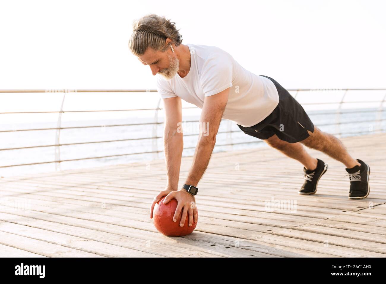 Image of sporty old man in sportswear using earpod while doing exercise ...