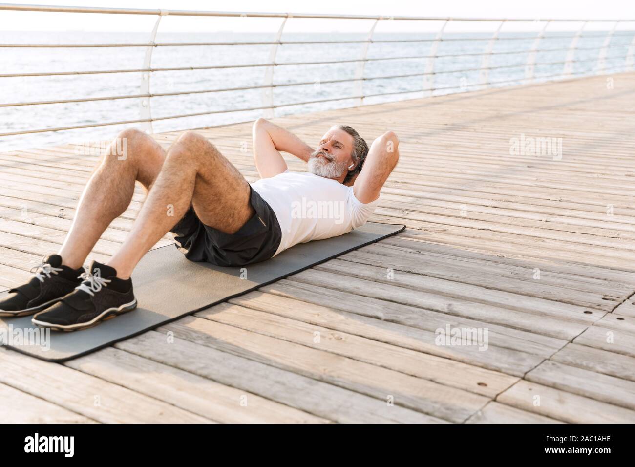 Image of calm old man in sportswear using earpod while doing exercise ...