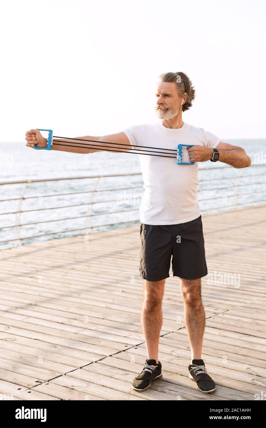 Image of strong elderly man in sportswear using earpod while doing ...