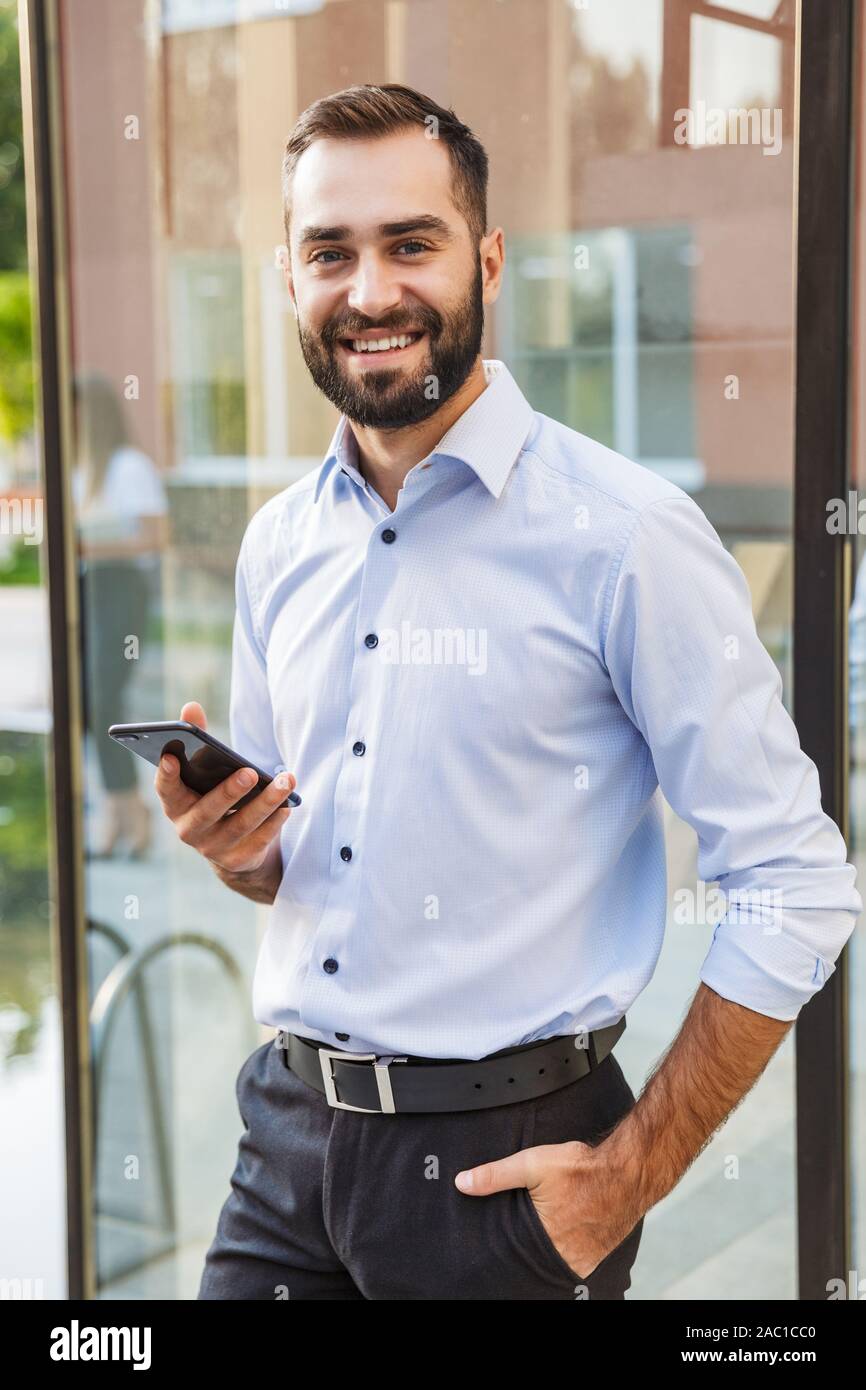 Photo of a young cheerful positive happy man outside at the street near ...