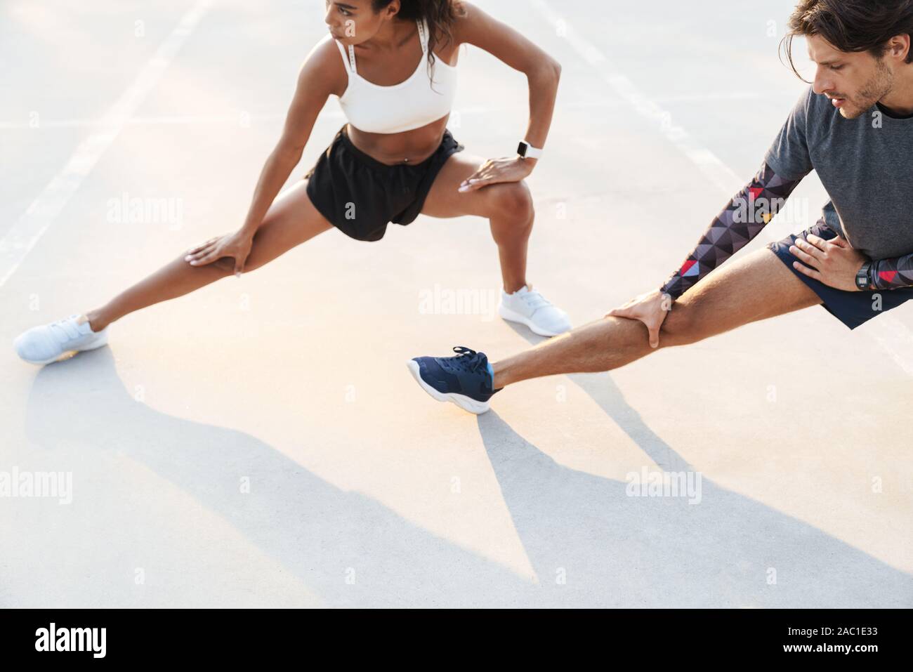 Photo of strong multinational couple in sportswear stretching their ...