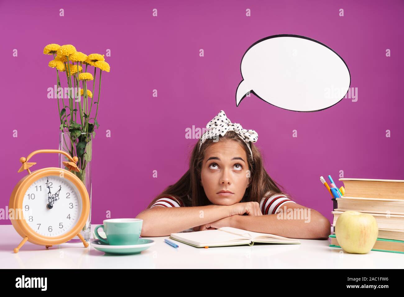 Attractive tired young girl sitting at the desk isolated over pink ...