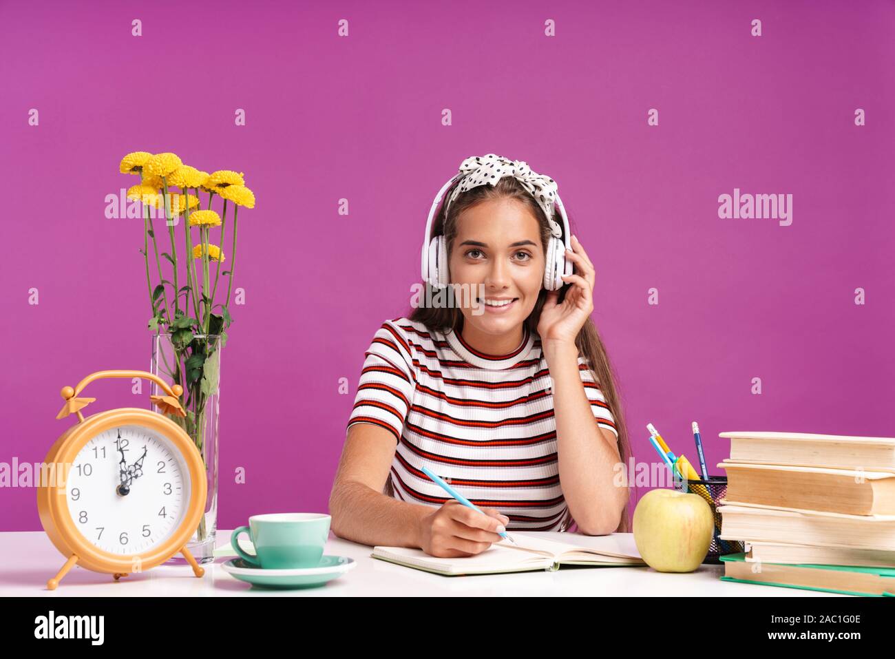 Image of nice smiling girl writing at notebook and using headphones ...