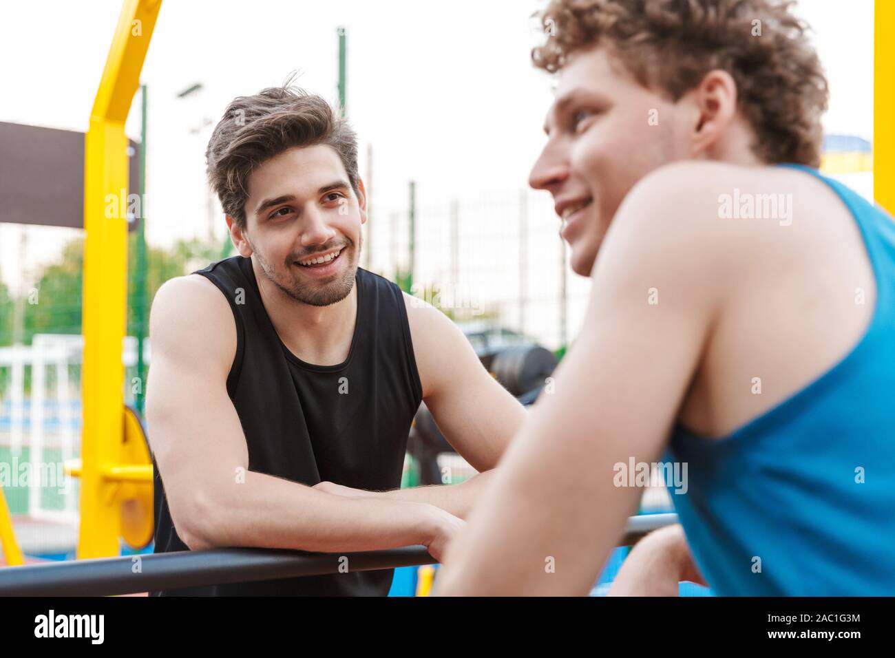 Two happy fitness men working out outdoors at the playground, talking ...