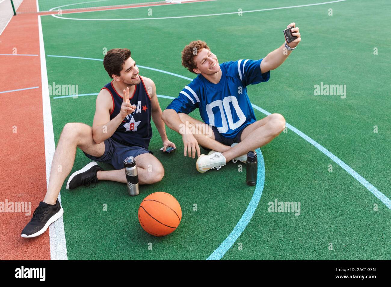 Two attarctive fit men basketball players sitting on a sports ground ...