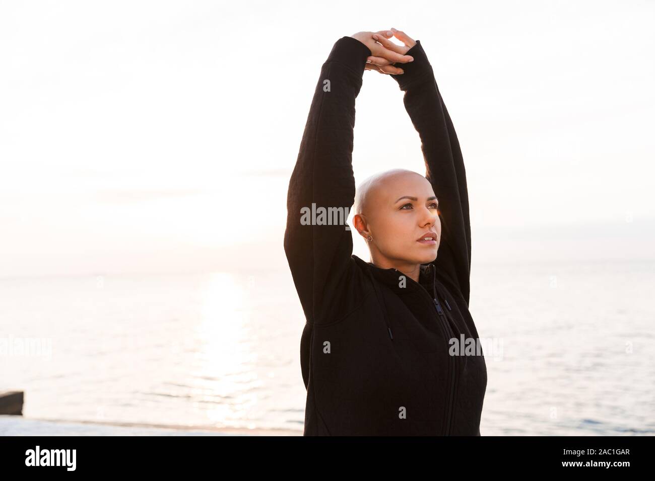 Image of focused bald woman in sportswear looking upward and stretching ...