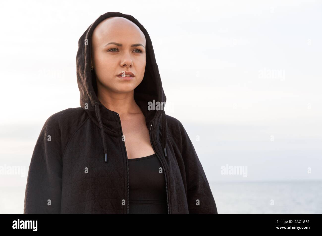Image of focused bald woman in black hood looking forward in sunny ...