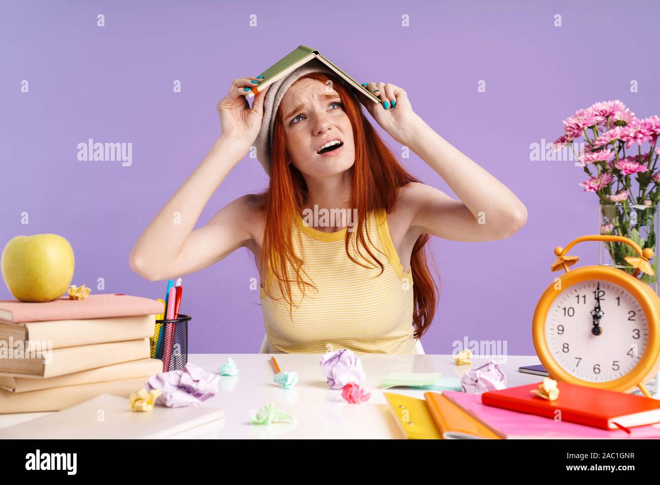Photo of confused student girl holding exercise book on her head while ...