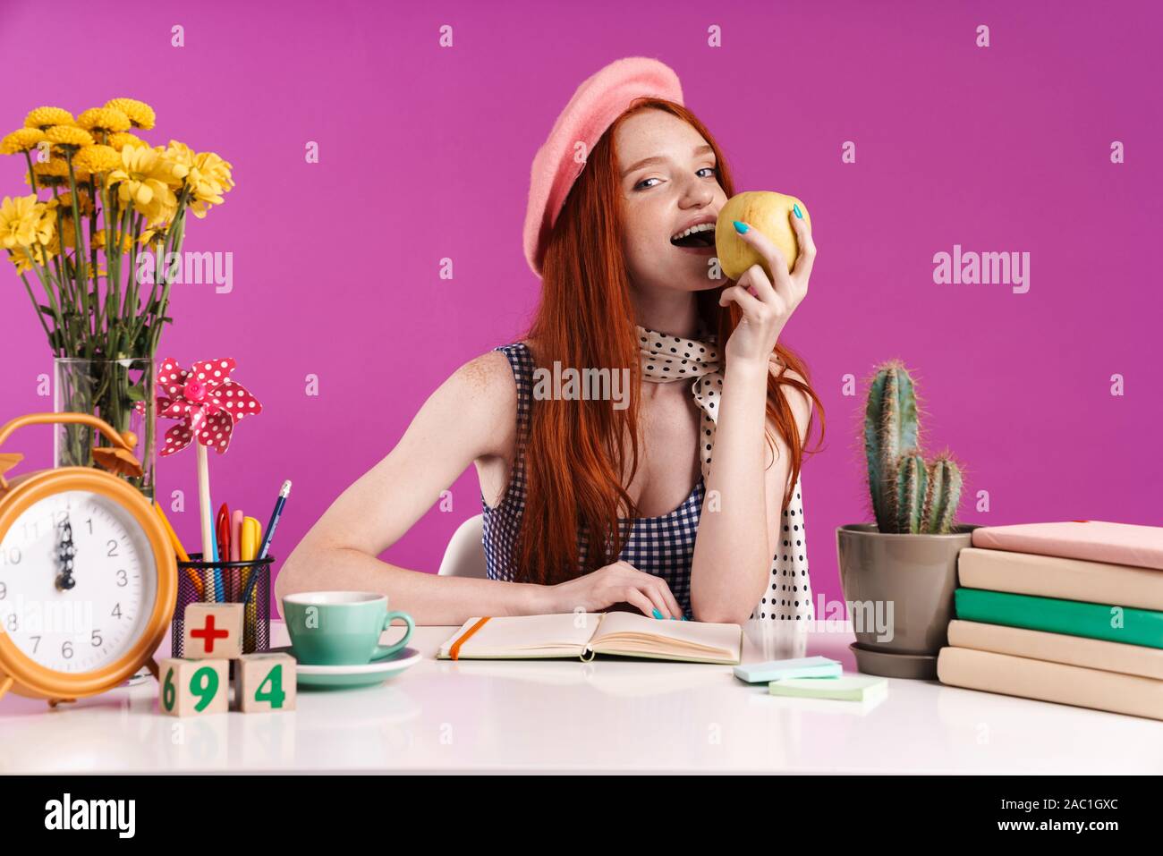 Photo of pleased student girl eating green apple while doing homework ...